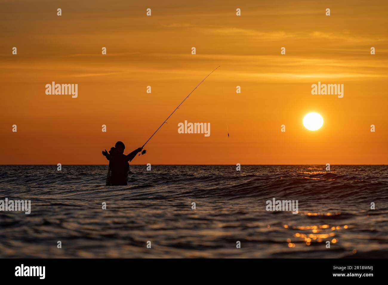 Dark silhouette of an angler in waterproof trousers fishing in front of ...