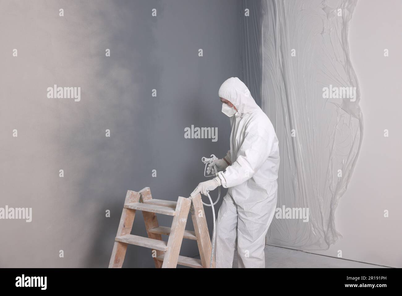 Decorator with spray paint near ladder and walls indoors Stock Photo ...