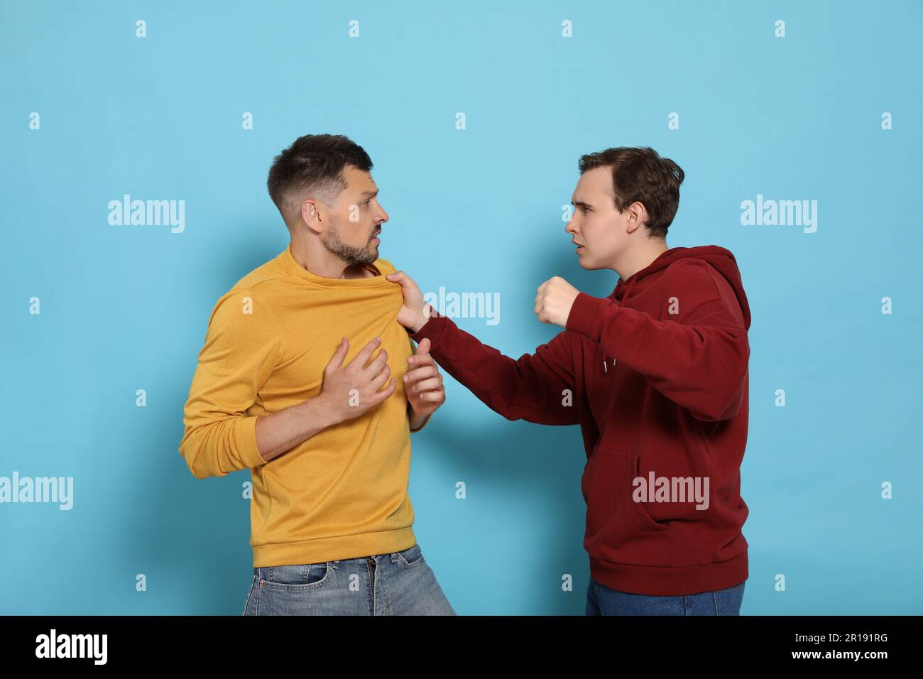 Two emotional men fighting on light blue background Stock Photo - Alamy