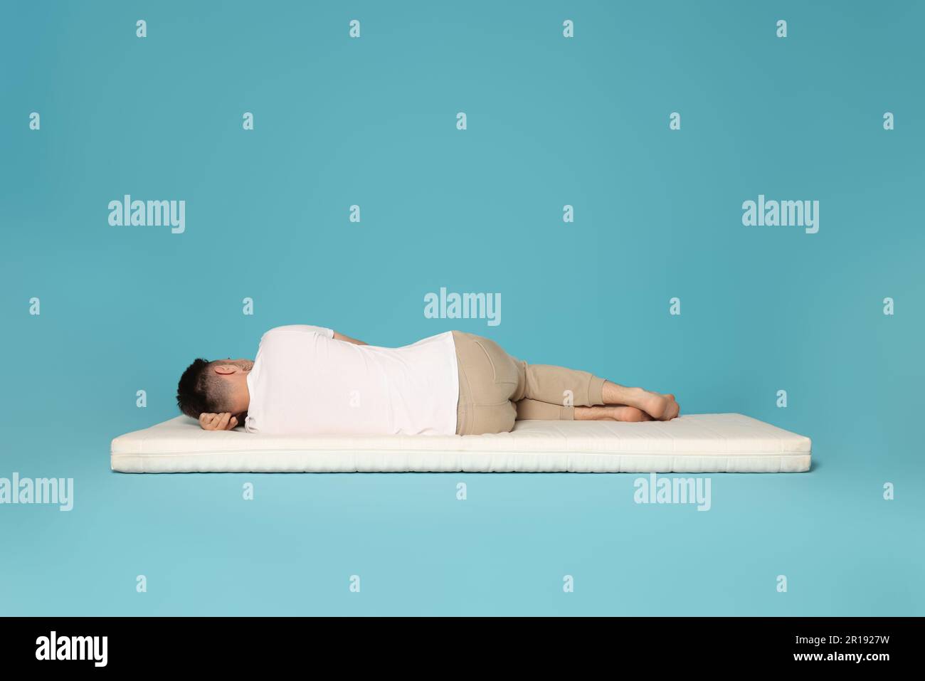 Man sleeping on soft mattress against light blue background, back view ...