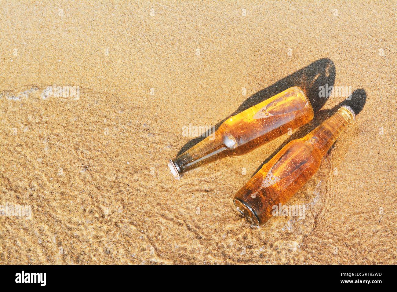Bottles of cold beer in water on sandy beach, above view. Space for ...