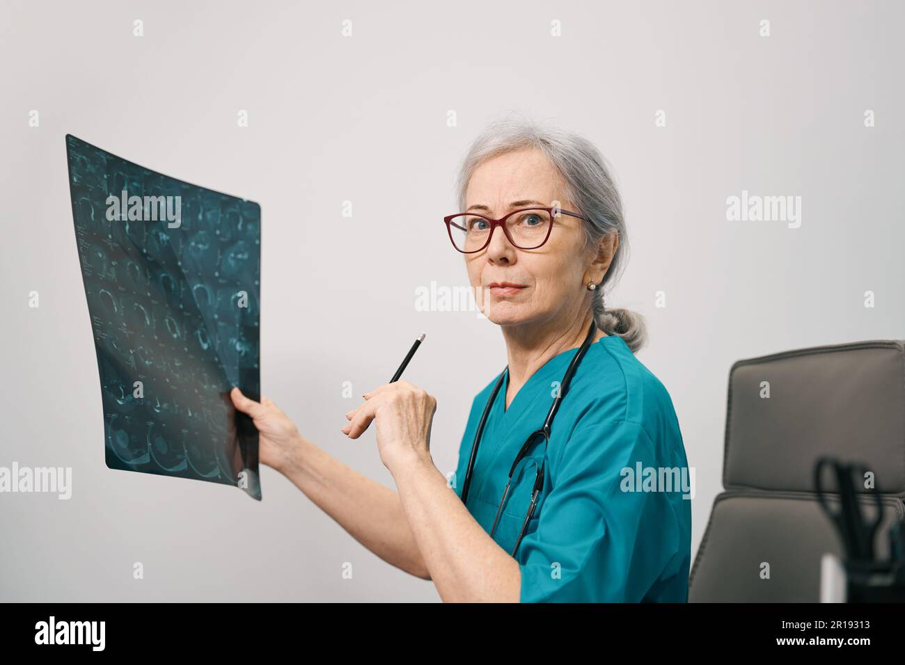Elderly medical worker holds an MRI scan of the brain in her hands ...