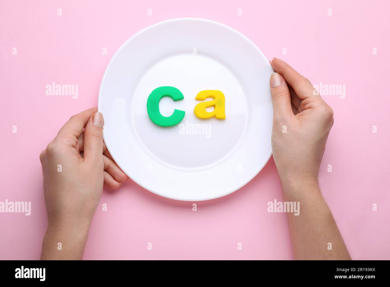 Woman holding plate with calcium symbol made of colorful letters on ...