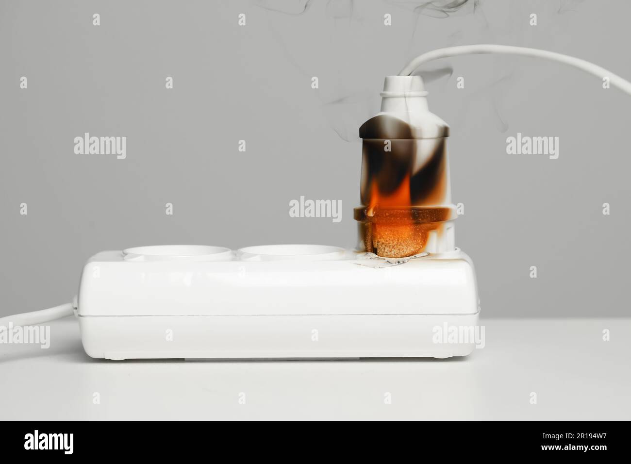 Inflamed plug in power strip on white table against grey wall ...
