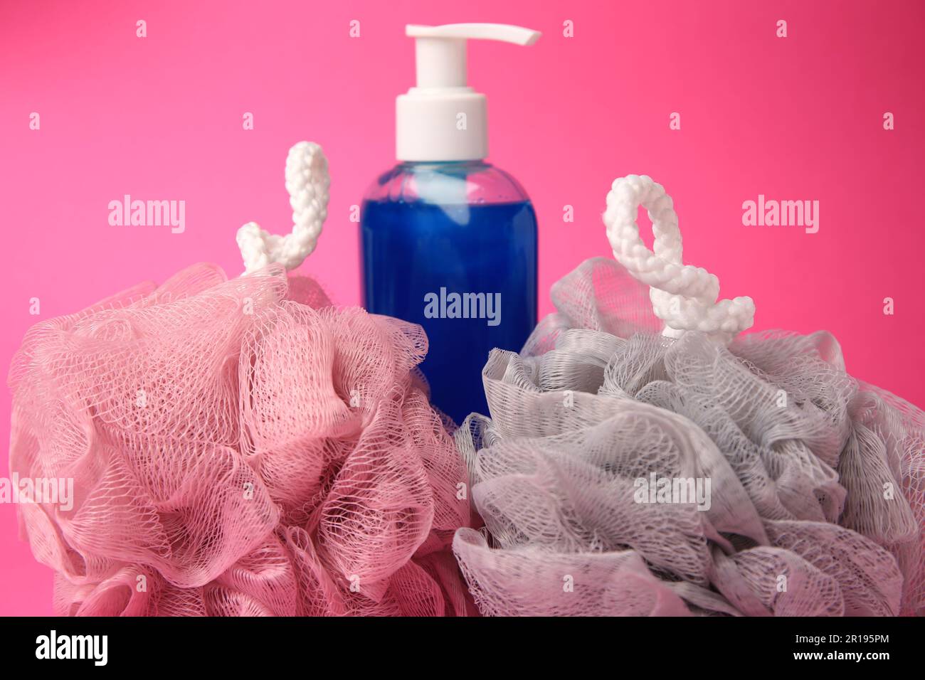 Colorful shower puffs and bottle of cosmetic product on pink background ...
