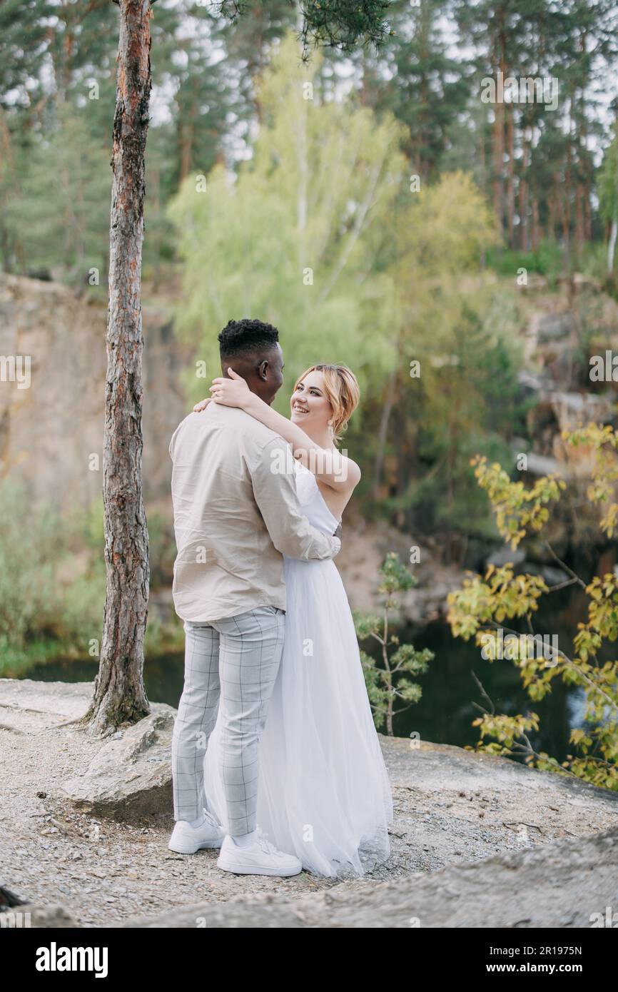 Happy interracial couple newlyweds stands, embraces and smiles against ...
