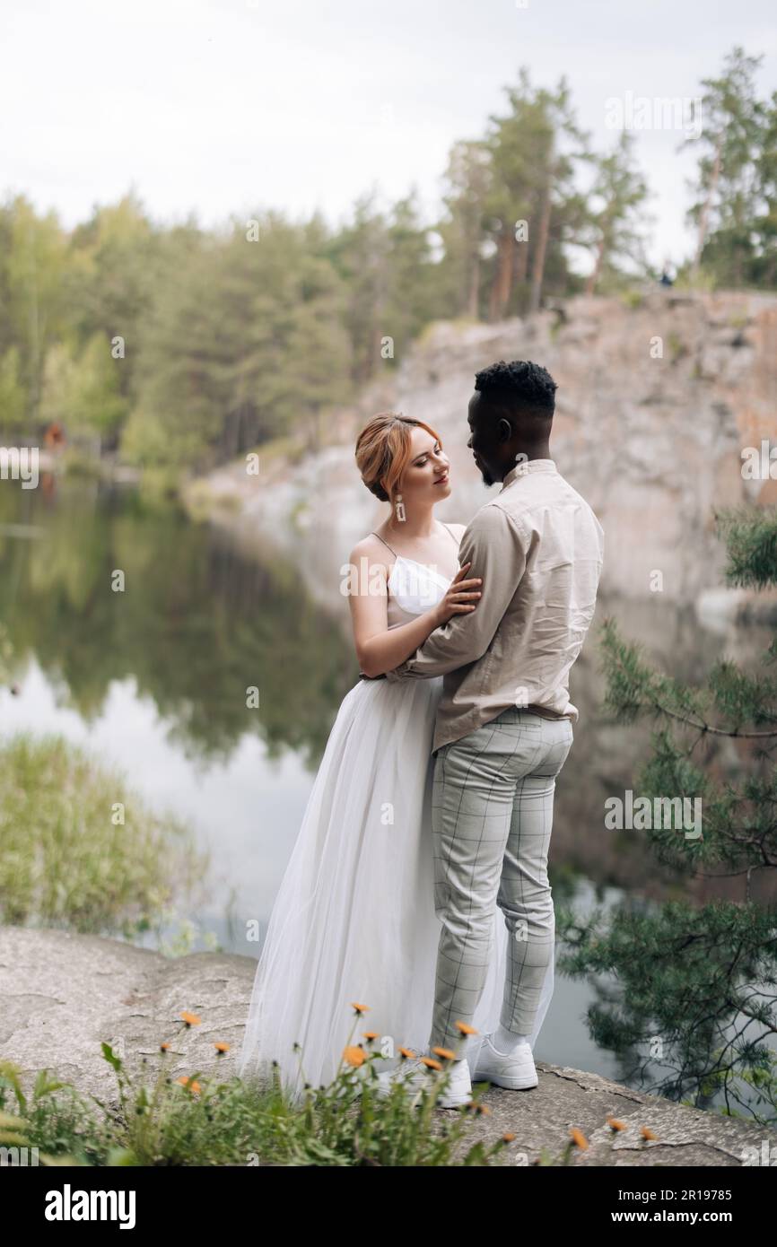 Happy Interracial Couple Newlyweds Stands On Rock And Embraces Against