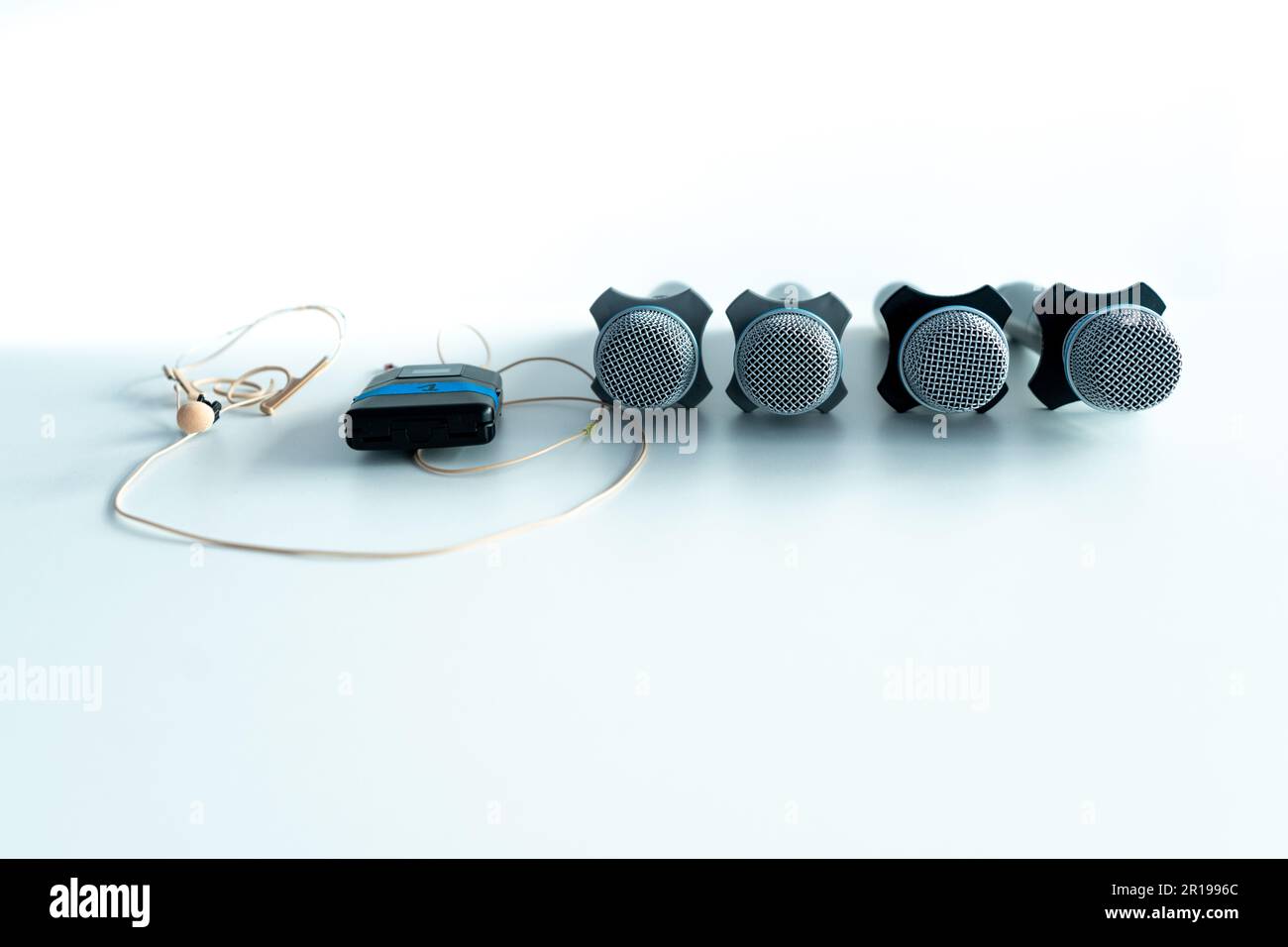 Three microphones in a row connected by a wire on a plain white ...