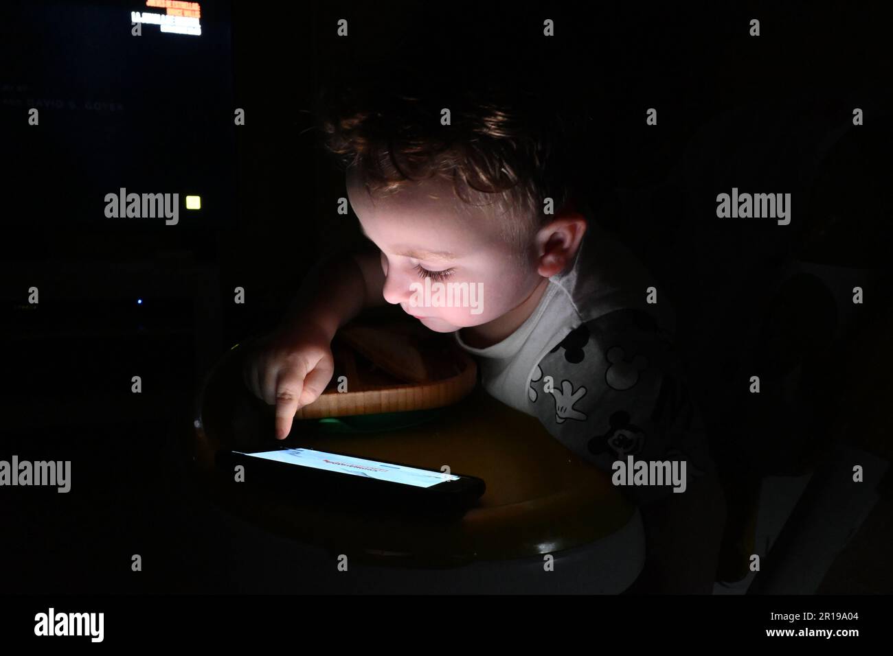 Child is scared looks on the tablet in the dark night. Black background ...