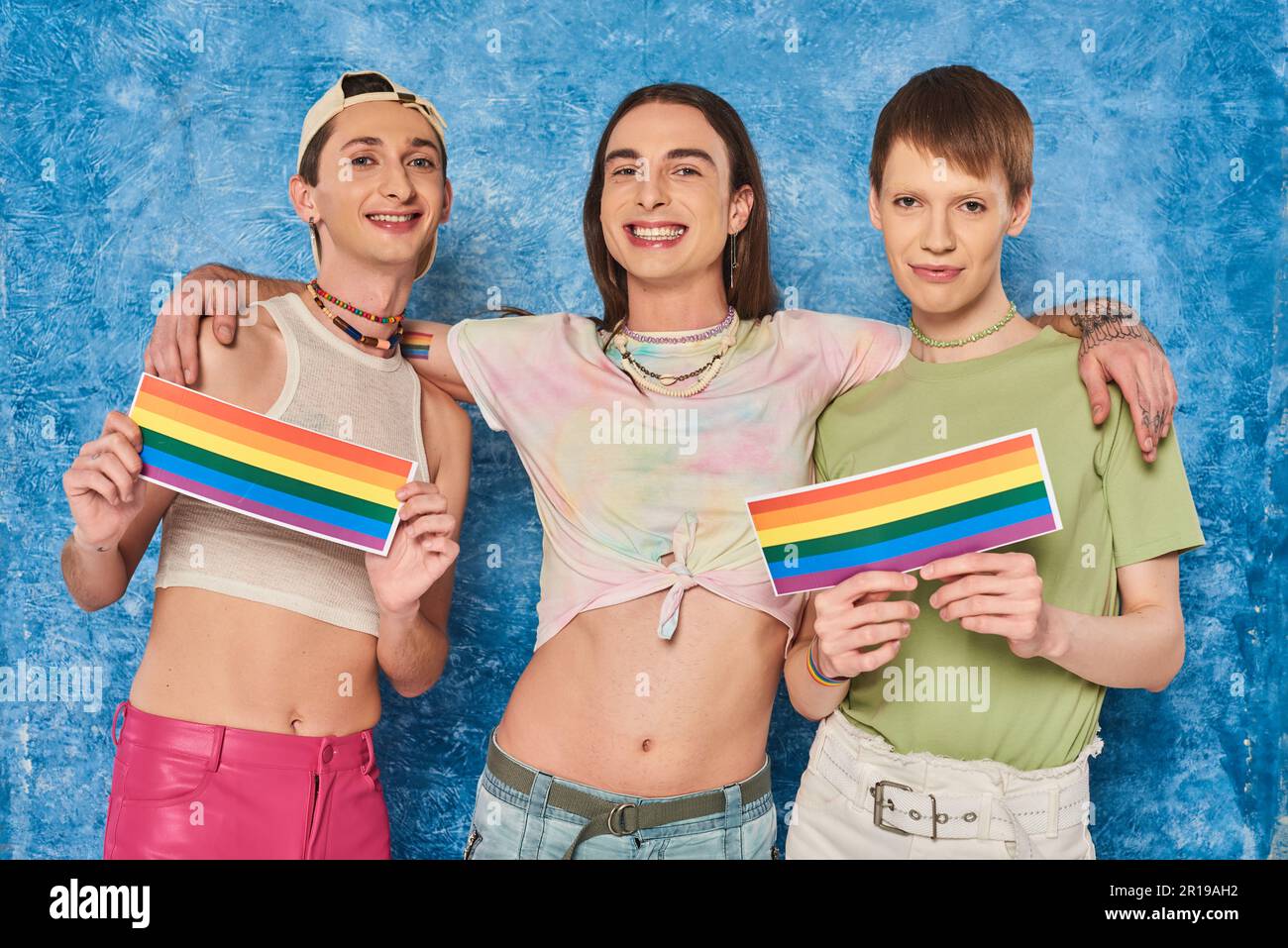 Positive and tattooed gay man hugging friends holding lgbt flags and ...