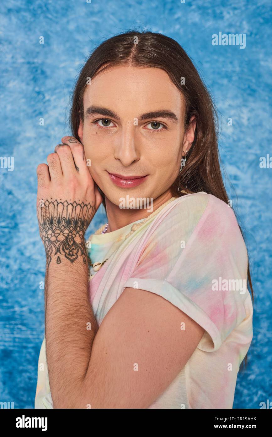 Portrait of young long haired and tattooed gay man looking at camera ...