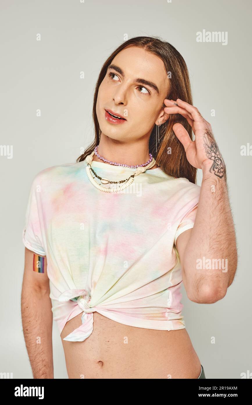 Dreamy and long haired homosexual man in tie dye t-shirt touching hair ...