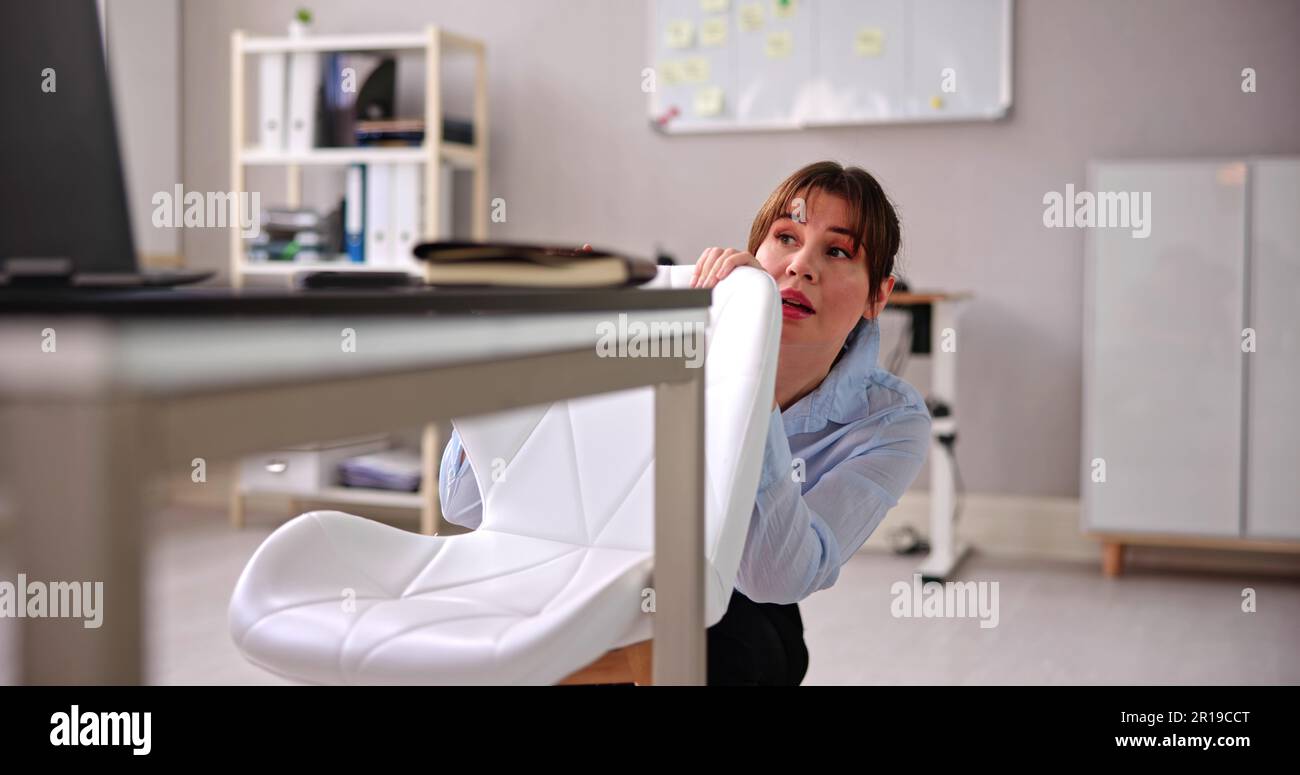 Scared Woman Hiding Behind Chair And Under Desk Stock Photo - Alamy
