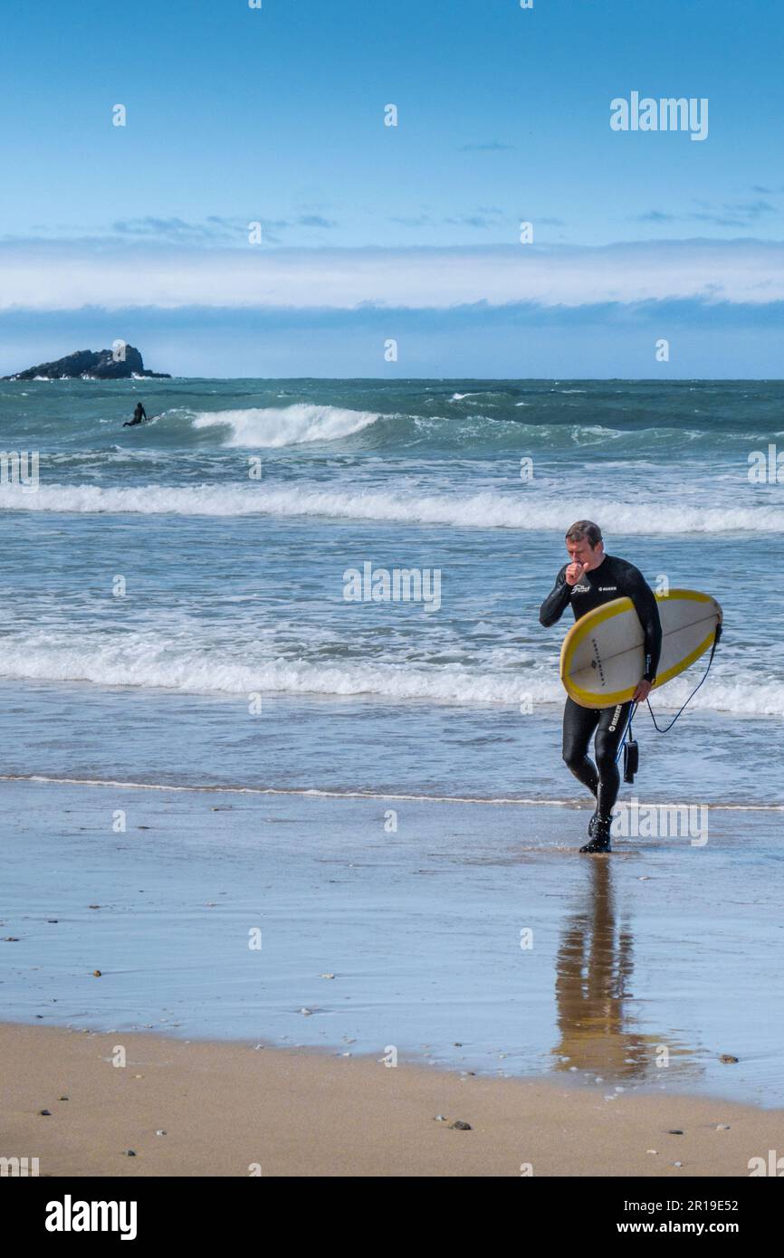 A male surfer carrying his surfboard and walking out of the sea after ...