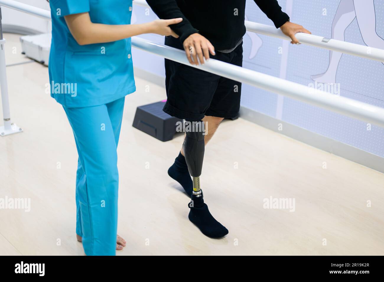 Physiotherapist helping patient with prosthetic leg at parallel bars ...