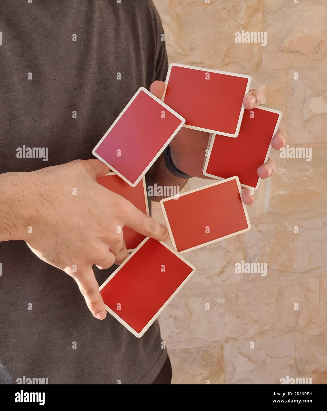 A young man performing a card trick with a deck of red playing cards ...