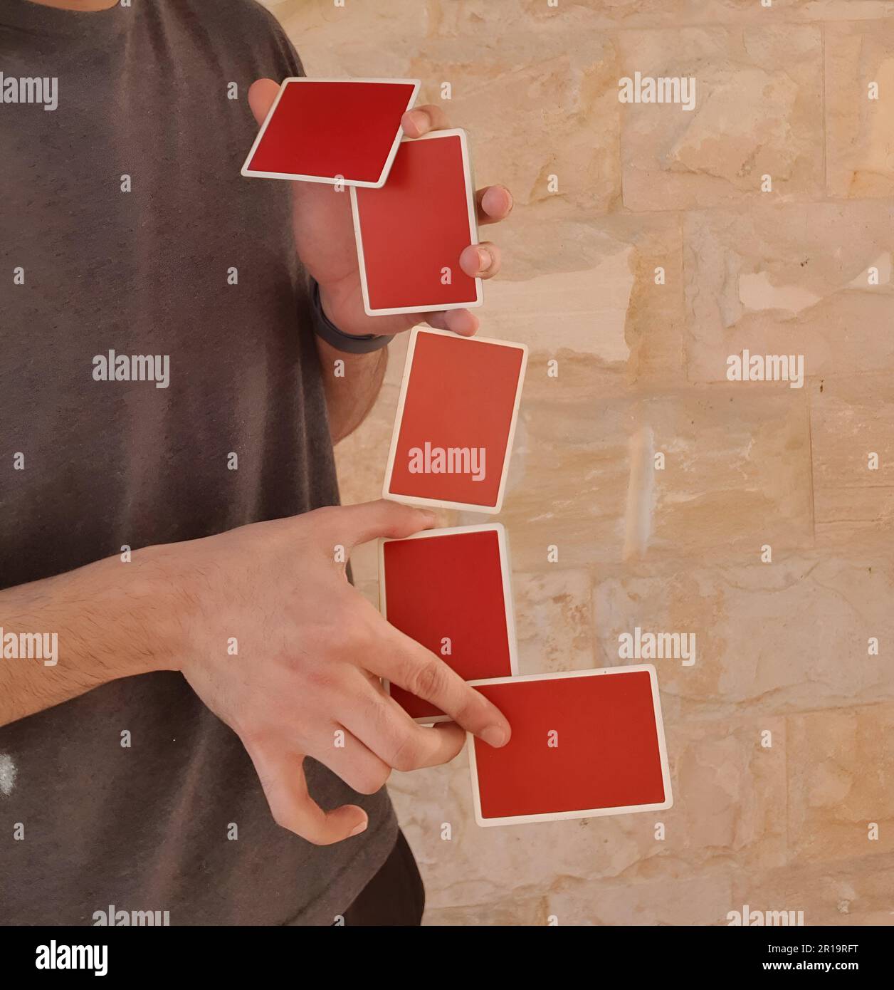 A young man performing a card trick with a deck of red playing cards ...