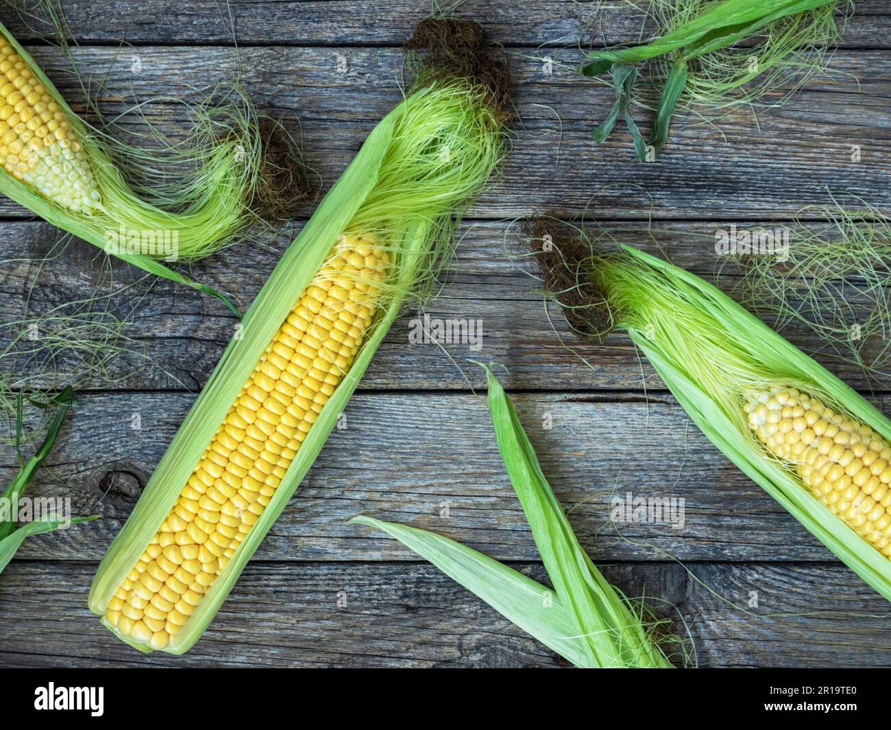 Fresh corn on the cob - a whole cob with leaves on wooden background in ...