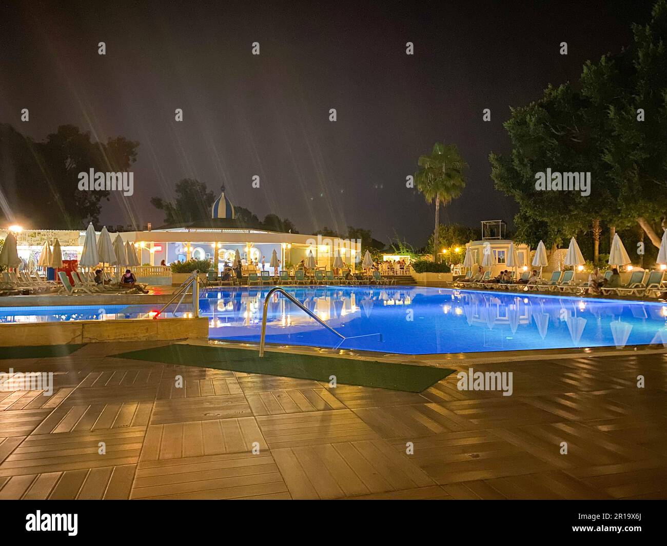 Beautiful night swimming pool with umbrellas and deck chairs and palm ...