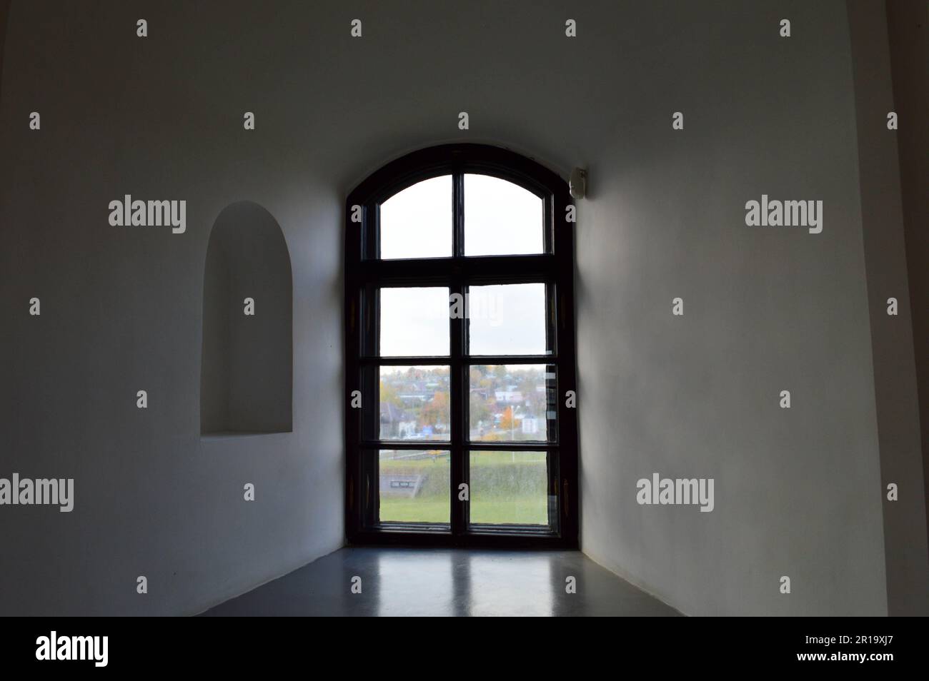 A small narrow black window with a frame on an old ancient stone white ...