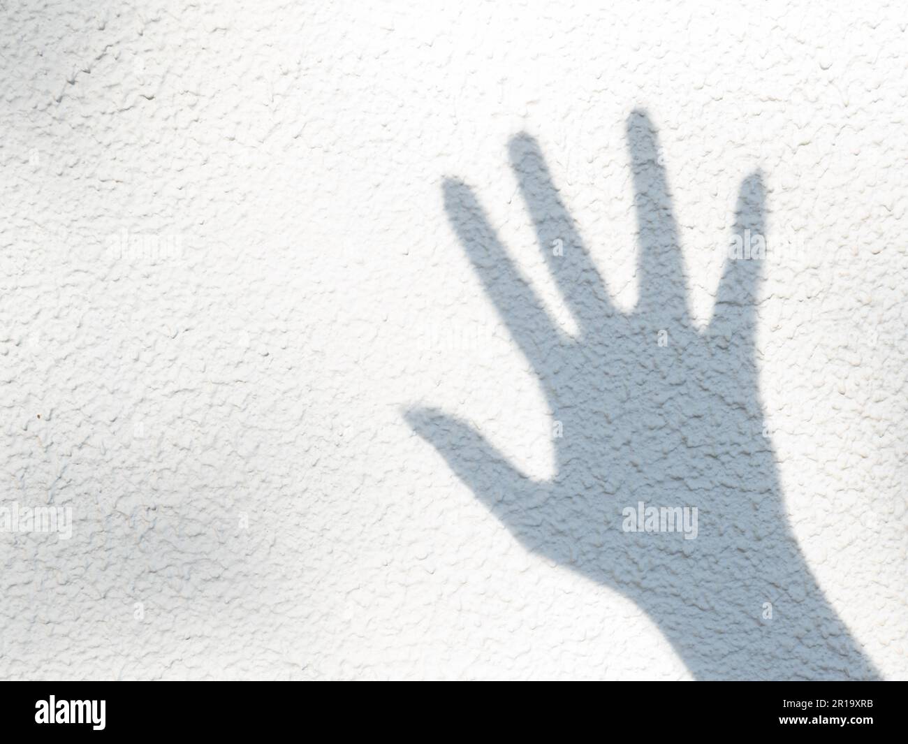 A hand shadow on white wall. Palm silhouette with outstretched fingers ...