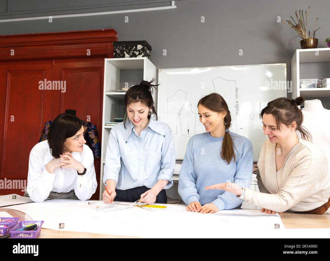 Four female fashion designers work together in a tailoring studio. A ...