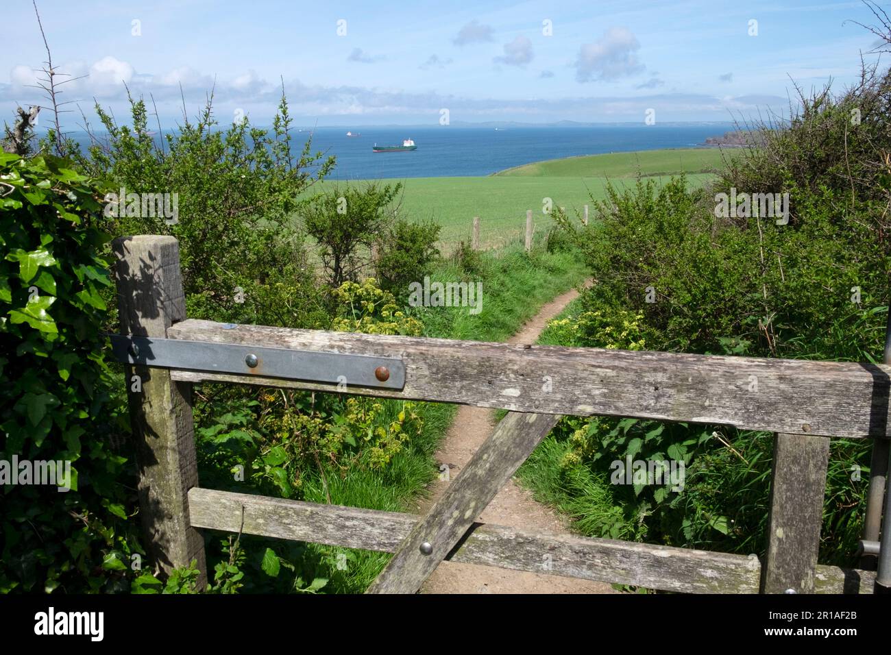 Footpath gate by green fields leading to Wales Coastal Path and view of ...