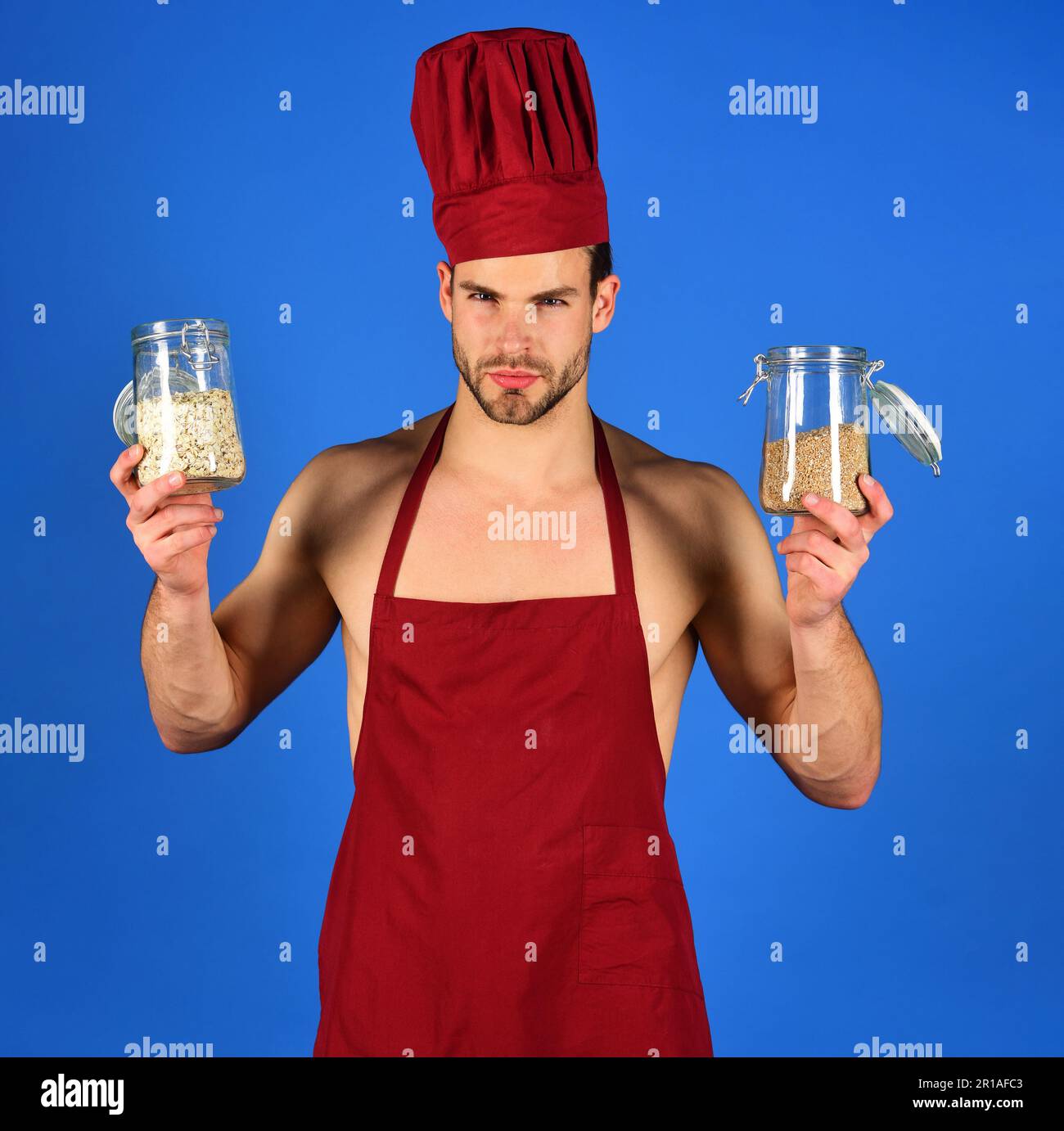 Professional male cook in chef hat and apron holds glass jars with ...