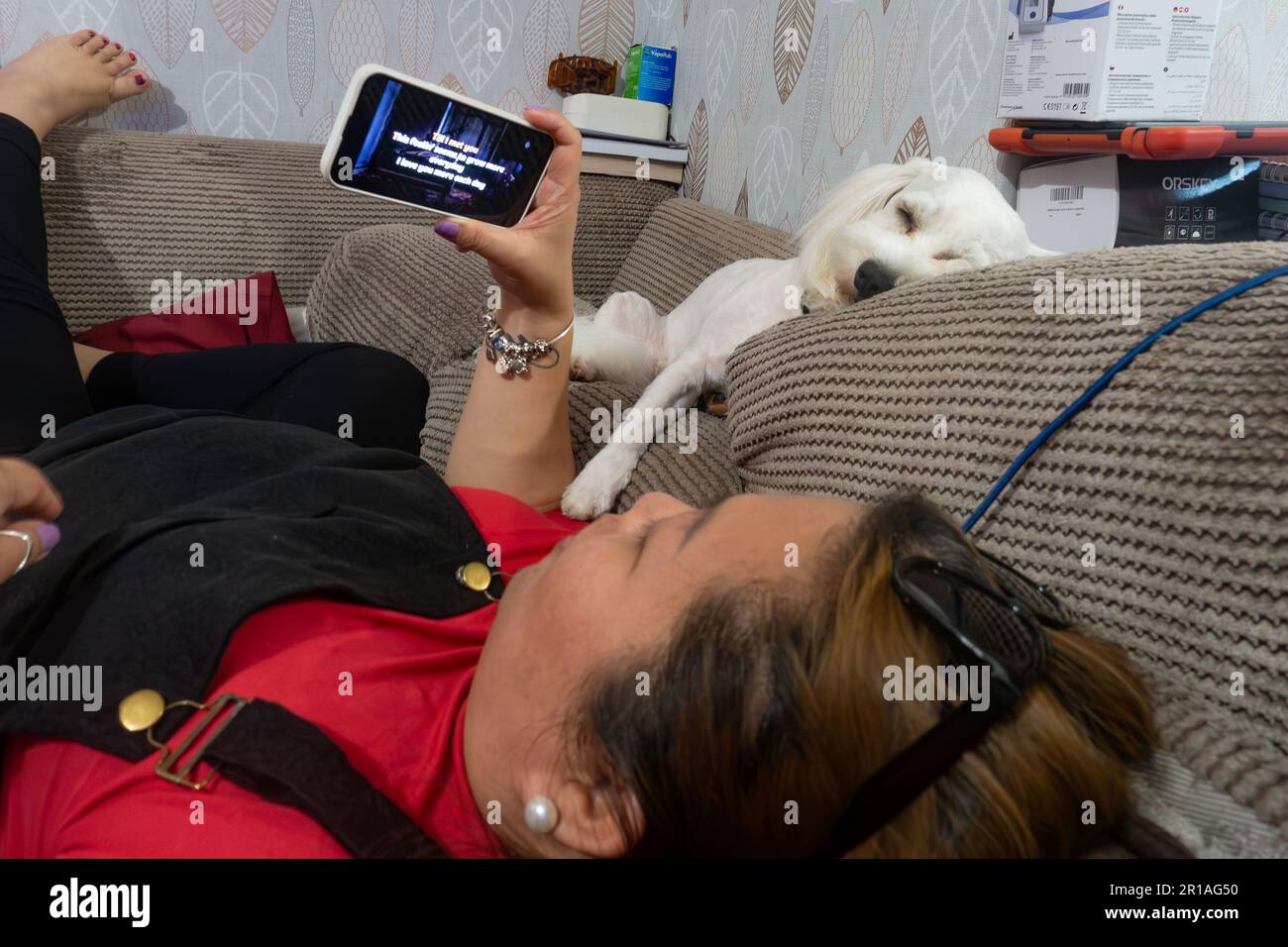 A lady relaxes on a settee in an evenign and watches videos on her ...