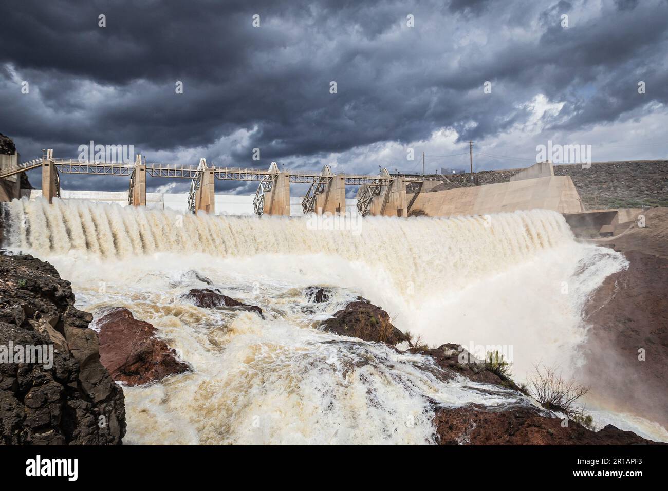 A dam with its flood gates open and a large volume of water flowing ...