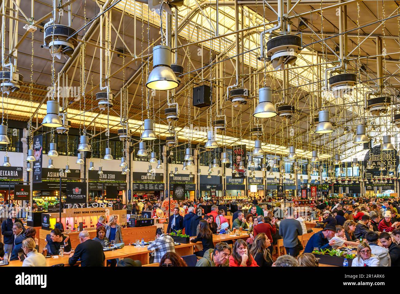 Large group of people having lunch in tables below electric lamps. Also ...