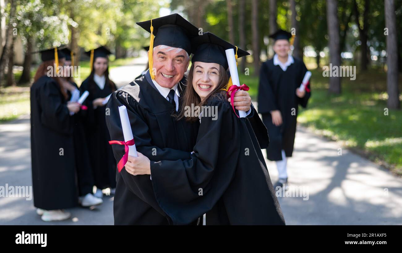 A group of graduates in robes outdoors. An elderly man and a young ...