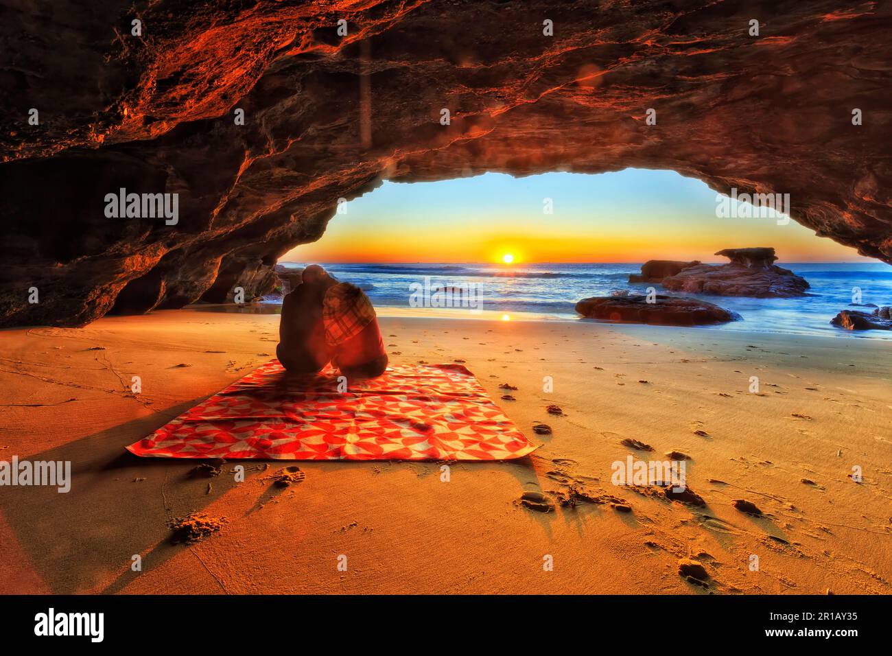 Unrecognisable couple of people facing sunrise over Pacific ocean from inside scenic sea cave in ...