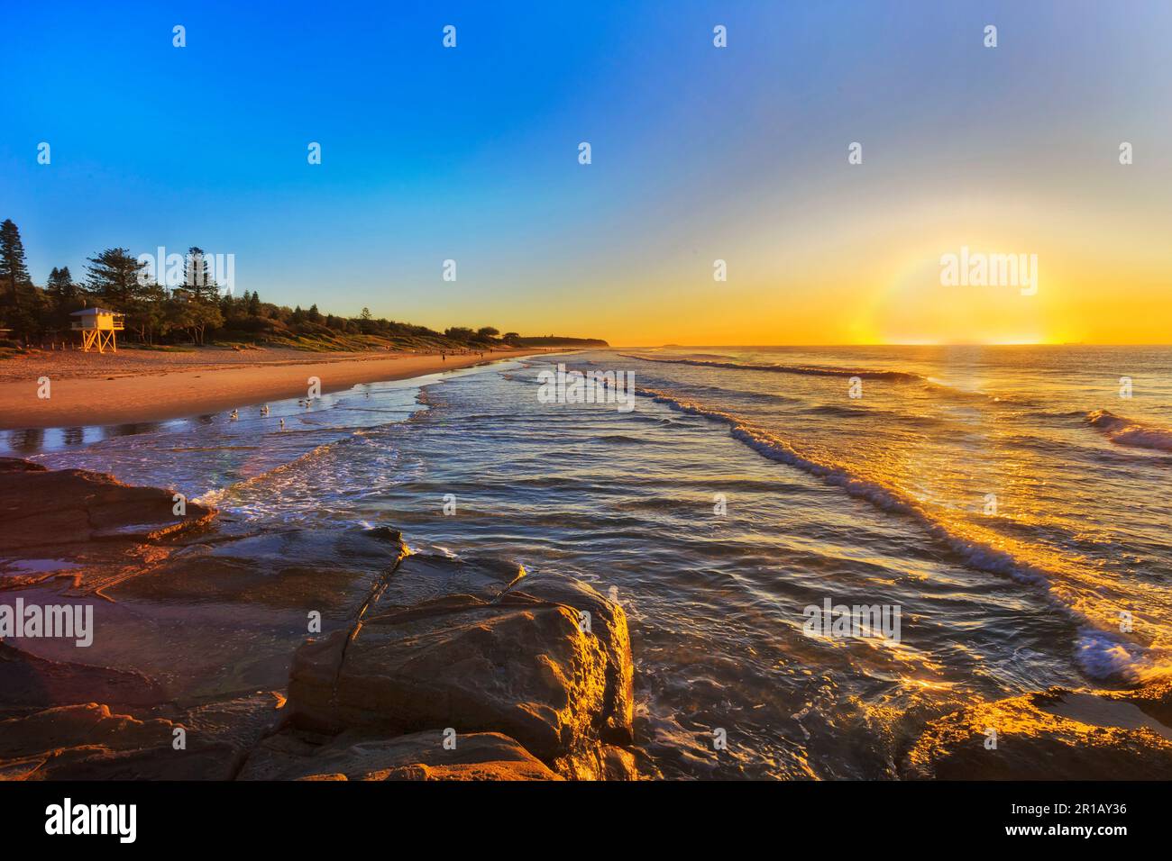 Colourful rising sun over Pacific ocean horizon off Caves beach sandy ...