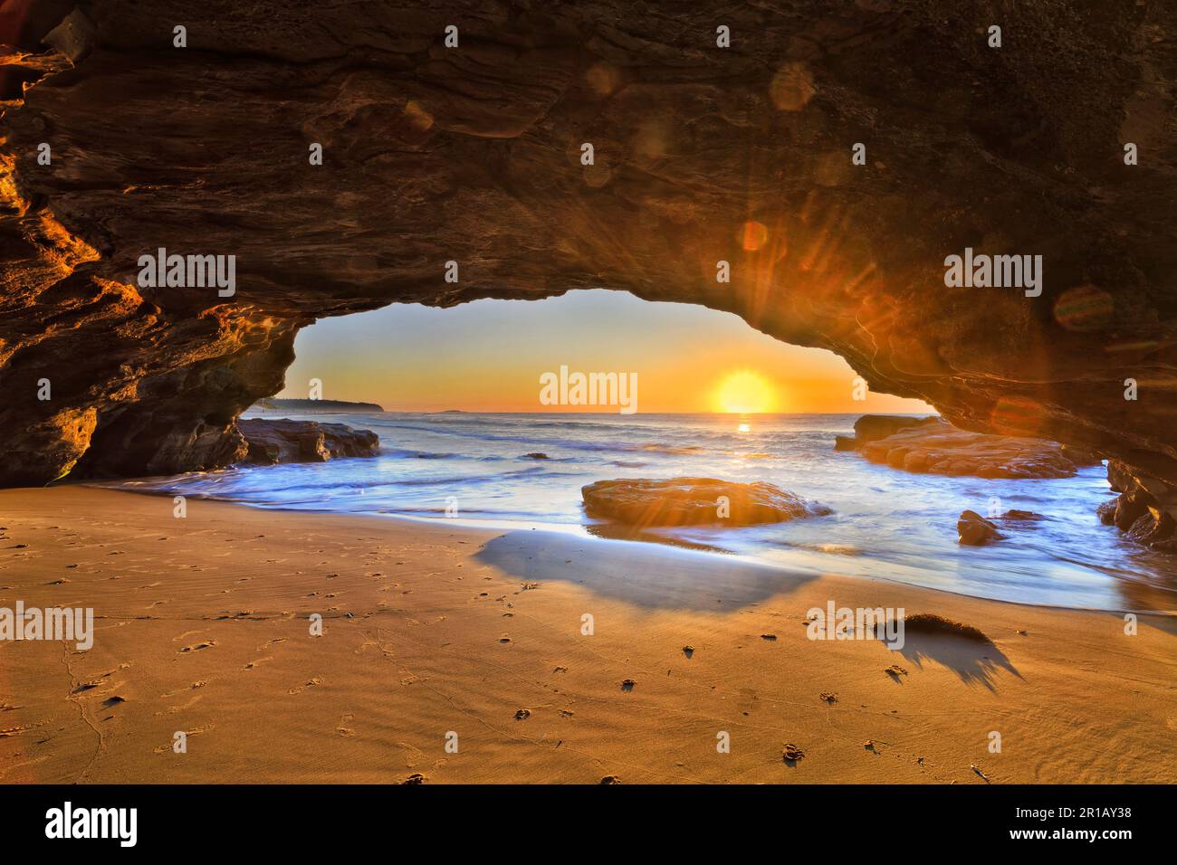 Bright rising sun over Pacific ocean horizon from inside sea cave in ...