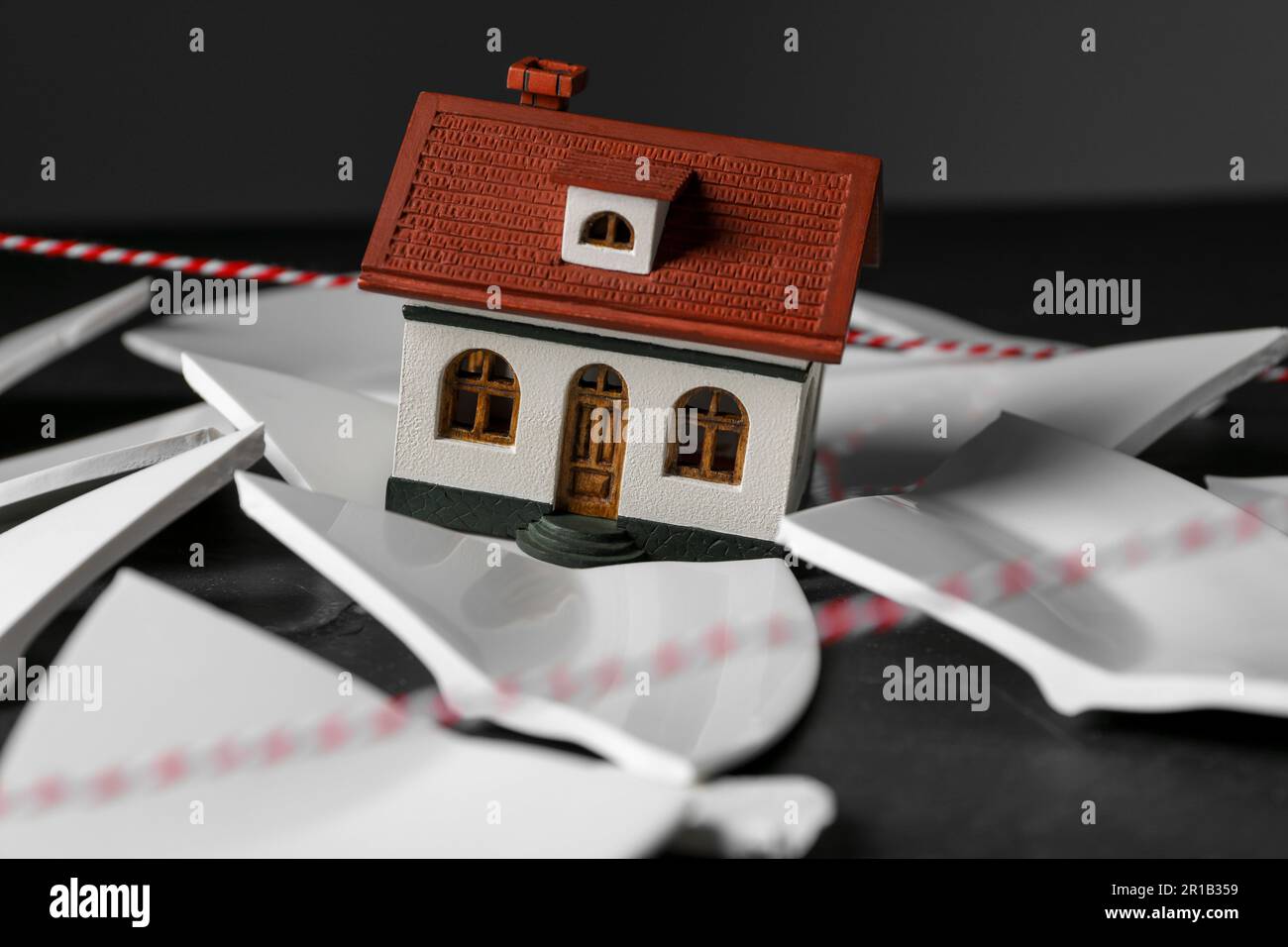 House model and broken dishes on black table depicting destruction ...