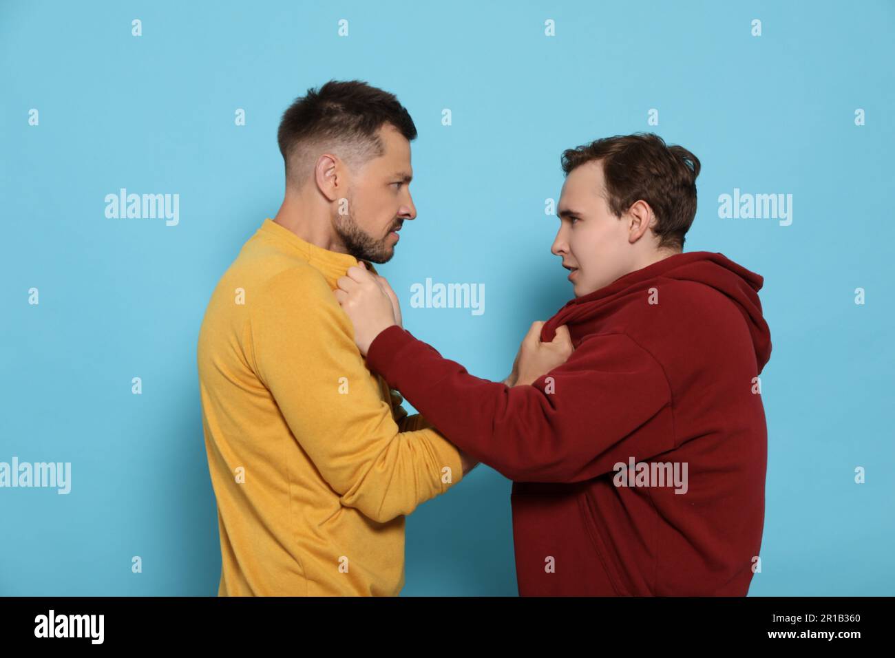 Two emotional men fighting on light blue background Stock Photo - Alamy