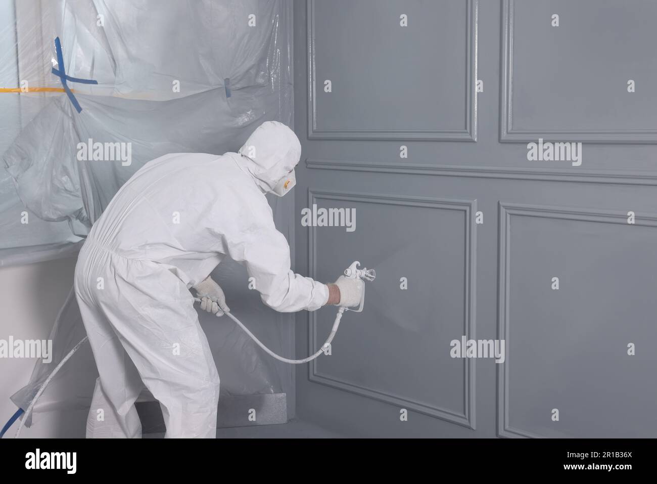 Decorator dyeing wall in grey color with spray paint, back view Stock ...