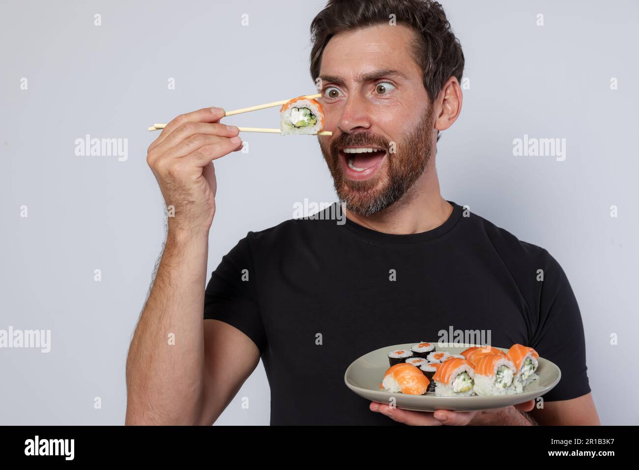 Emotional man eating tasty sushi roll and holding plate with food ...