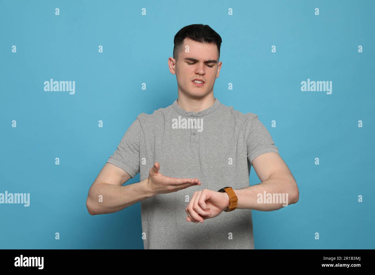 Emotional young man checking time on light blue background. Being late ...