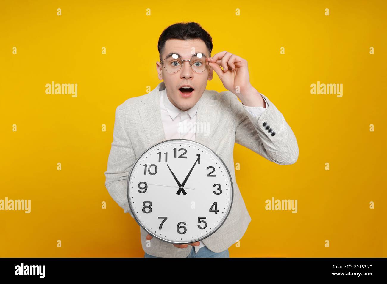 Emotional young man holding clock on orange background. Being late ...
