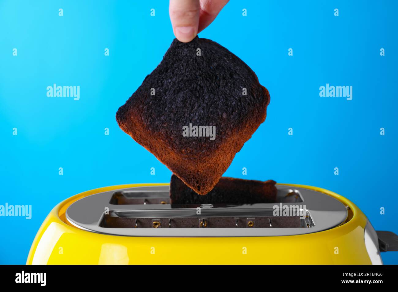 Woman taking off burnt bread from toaster against light blue background ...