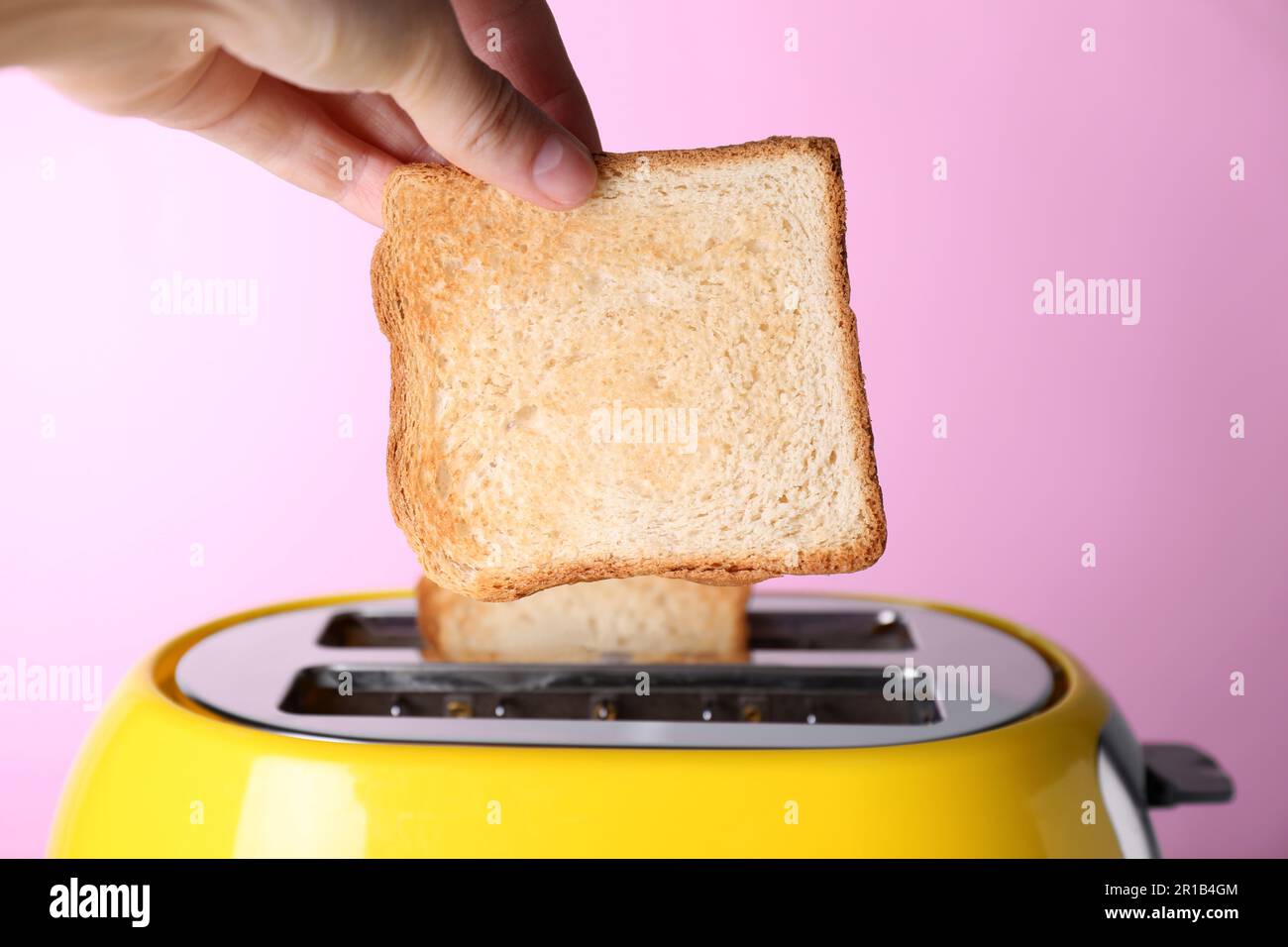 Woman taking off roasted bread from toaster against pale pink ...