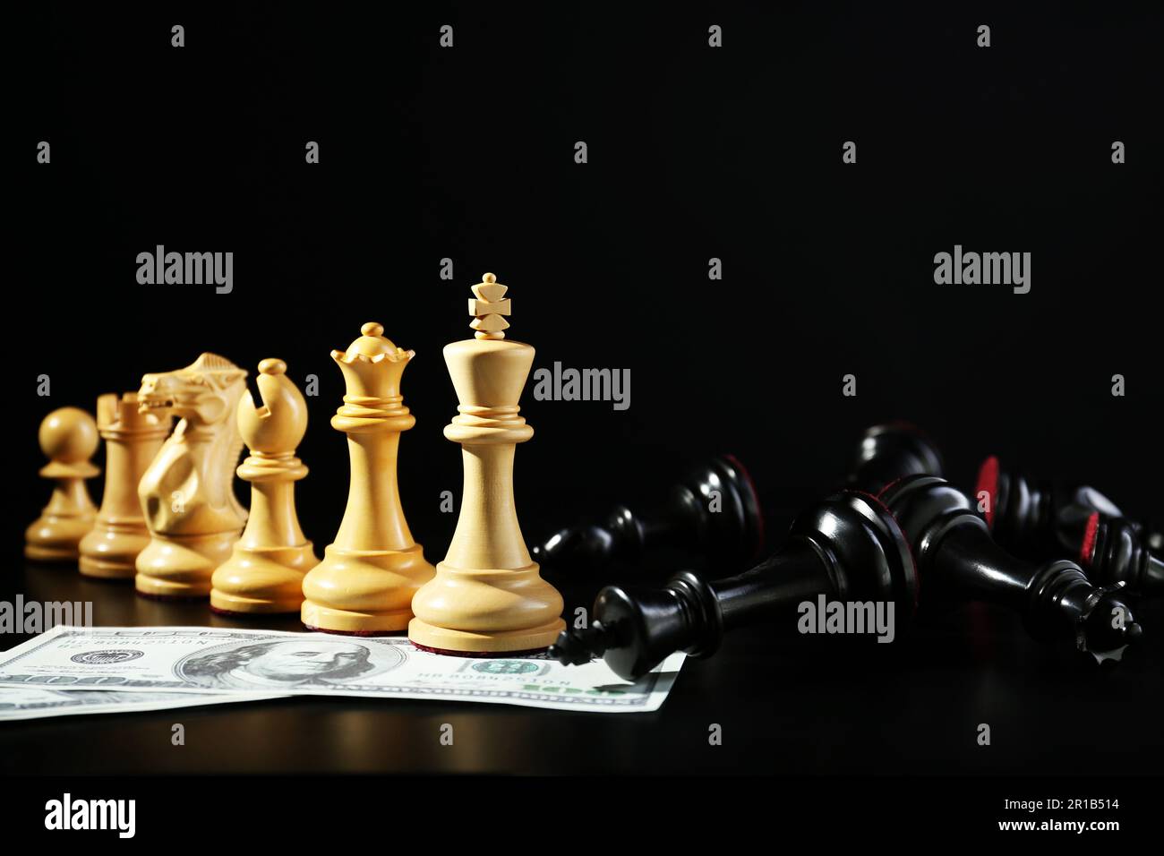 White chess pieces, black fallen ones and money against dark background ...