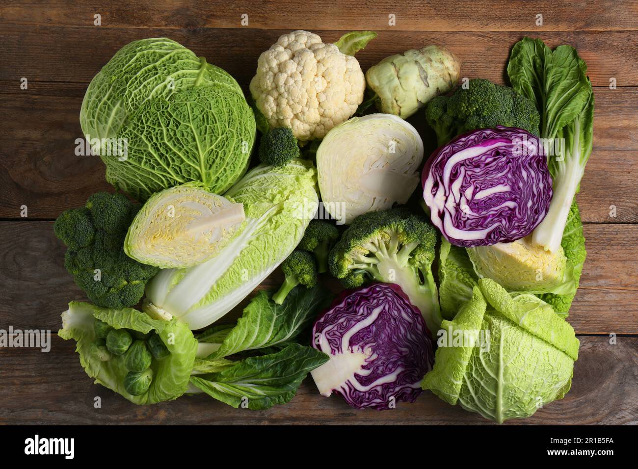 Different whole and cut types of cabbage on wooden table, flat lay ...