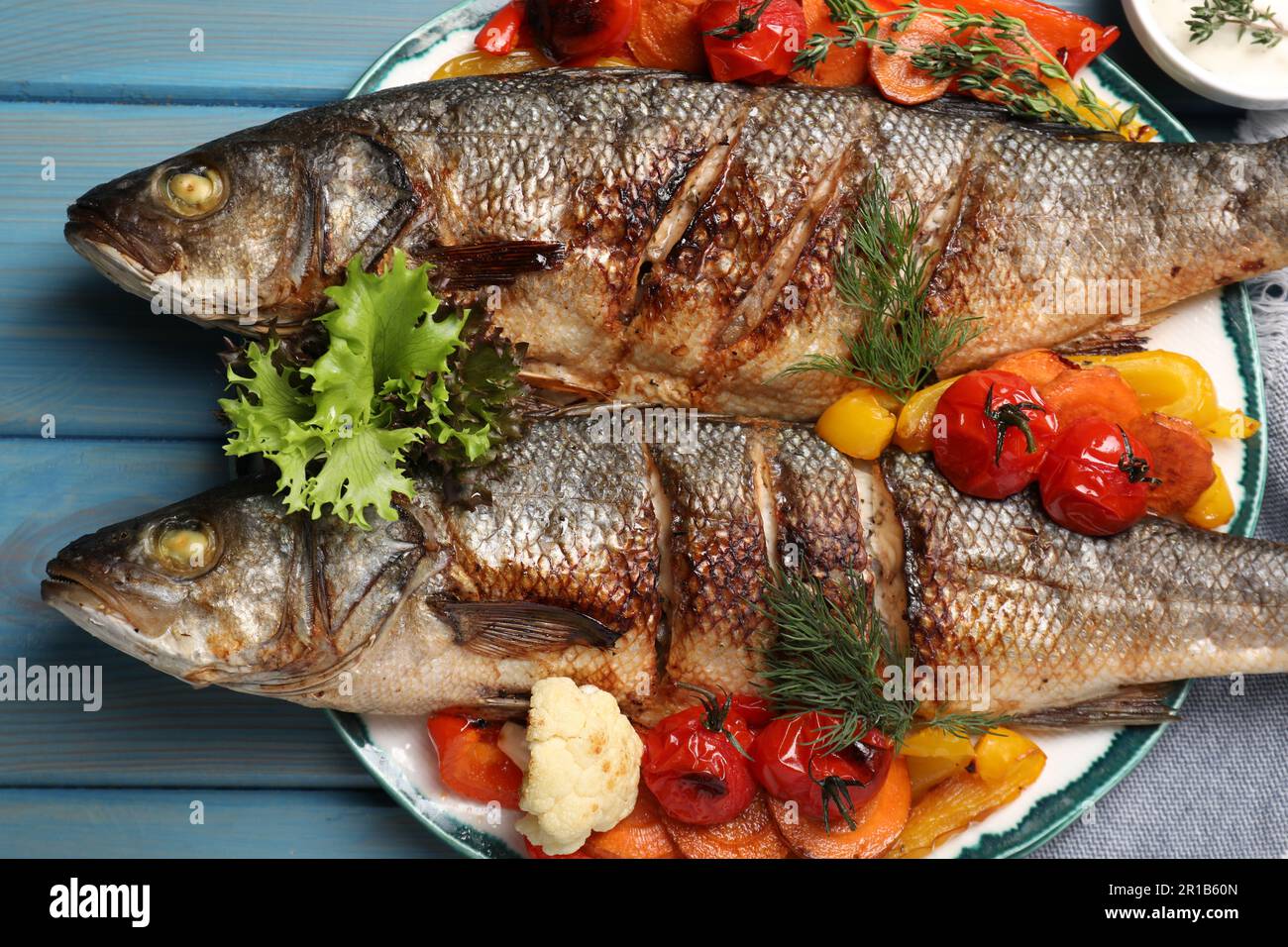 Plate with delicious roasted sea bass fish and vegetables on light blue ...