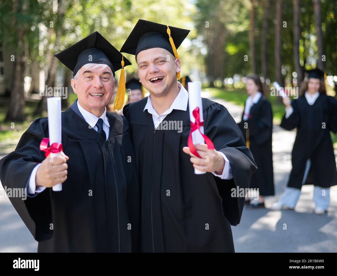 A group of graduates in robes outdoors. An elderly man and a young guy ...