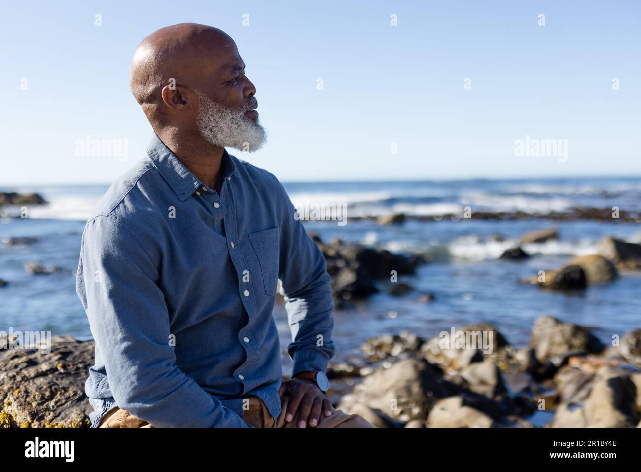 Thoughtful senior african american man sitting on rocks and admiring ...
