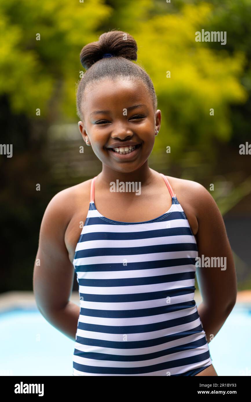 Portrait of happy african american girl in swimsuit standing by pool in ...