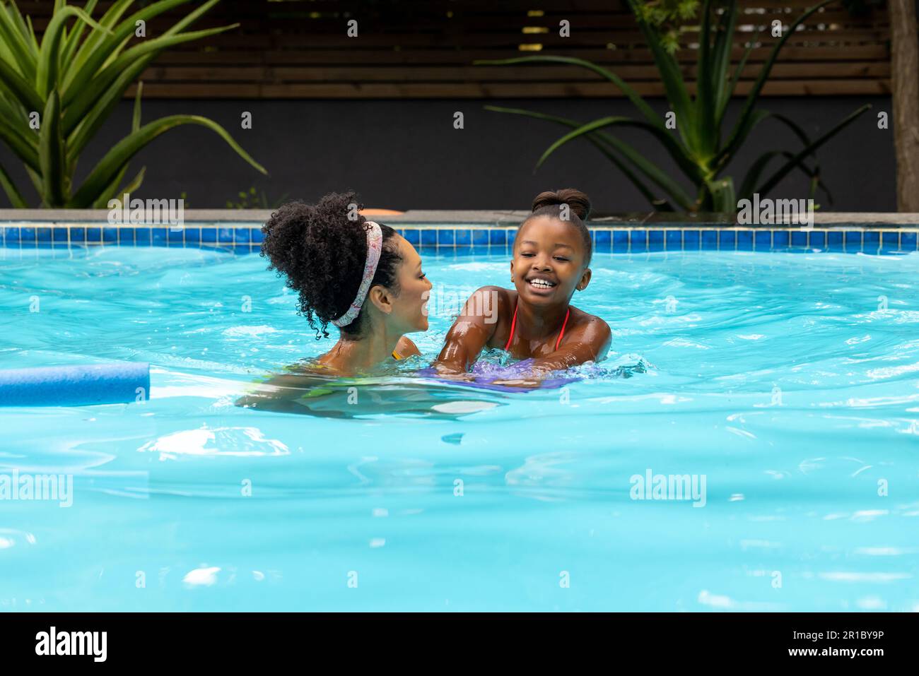 Happy african american mother teaching daughter to swim with float in ...